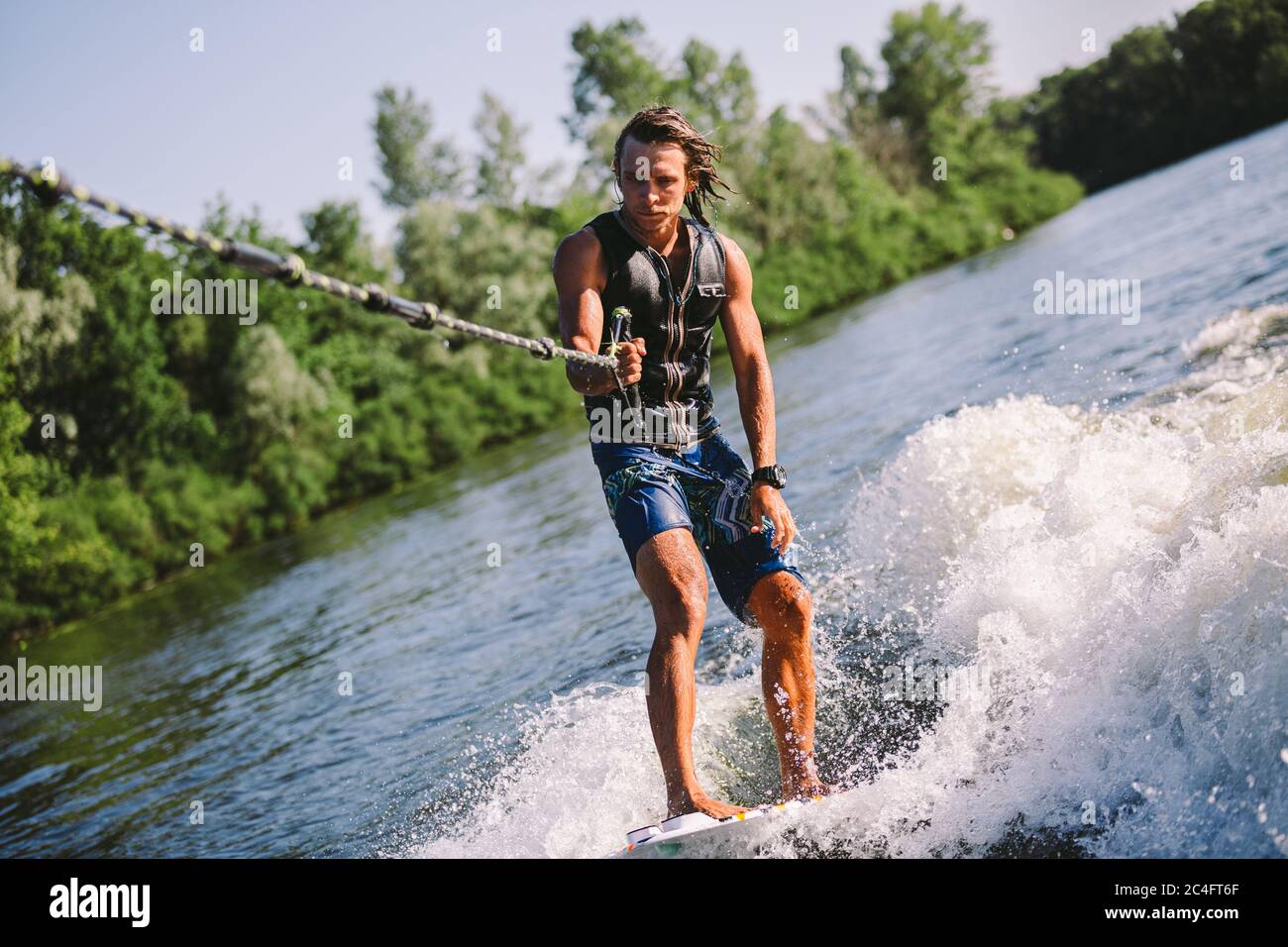 Active wakesurfer jumping on wake board down the river waves. Surfer on ...