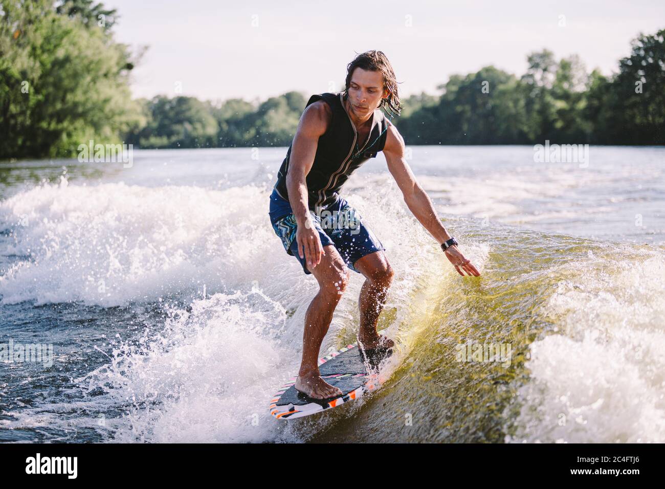 Beautiful long haired blond wakesurf in vest on board along waves of ...