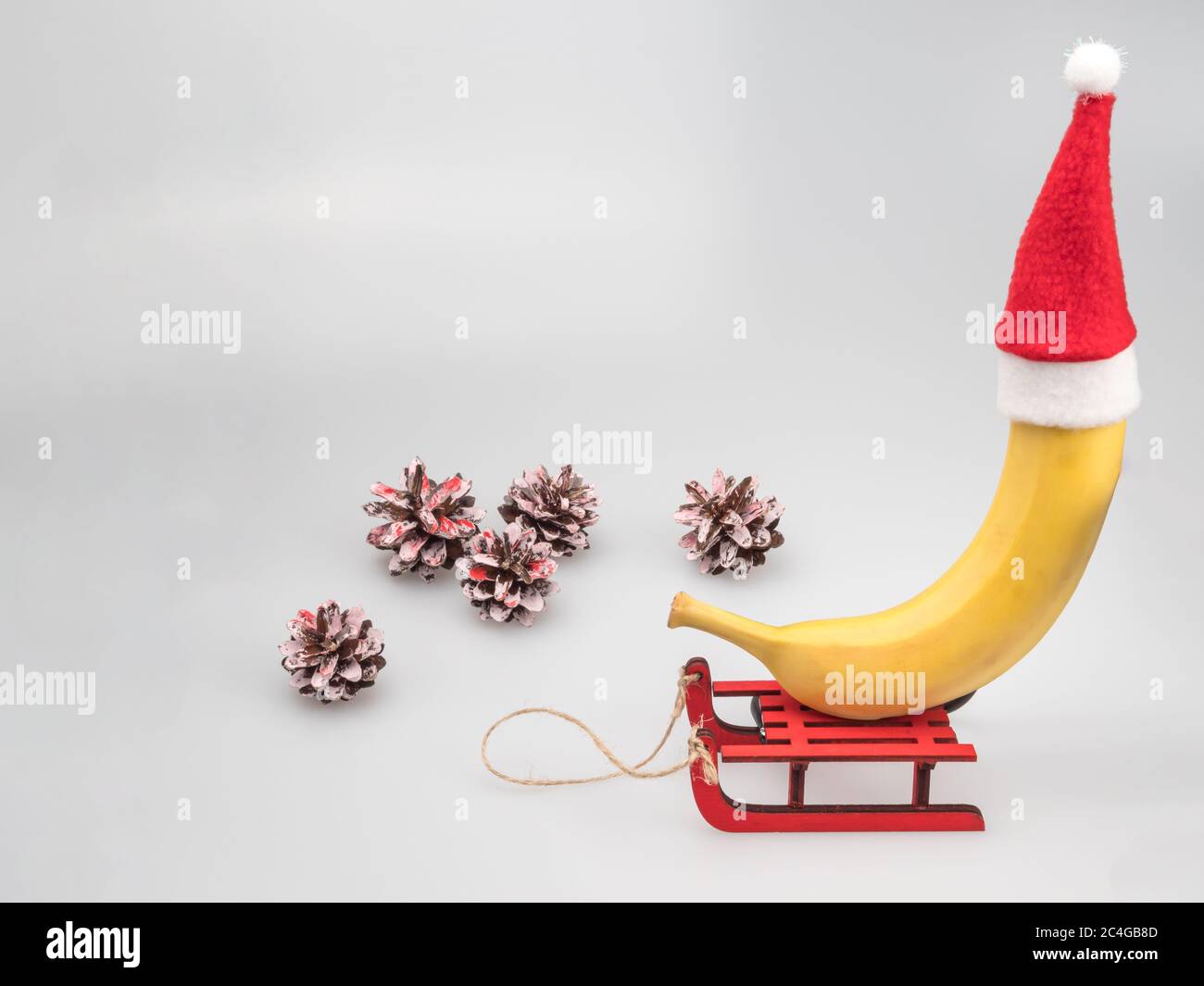 Banana in a Christmas hat on a sled. Festive cones Stock Photo - Alamy