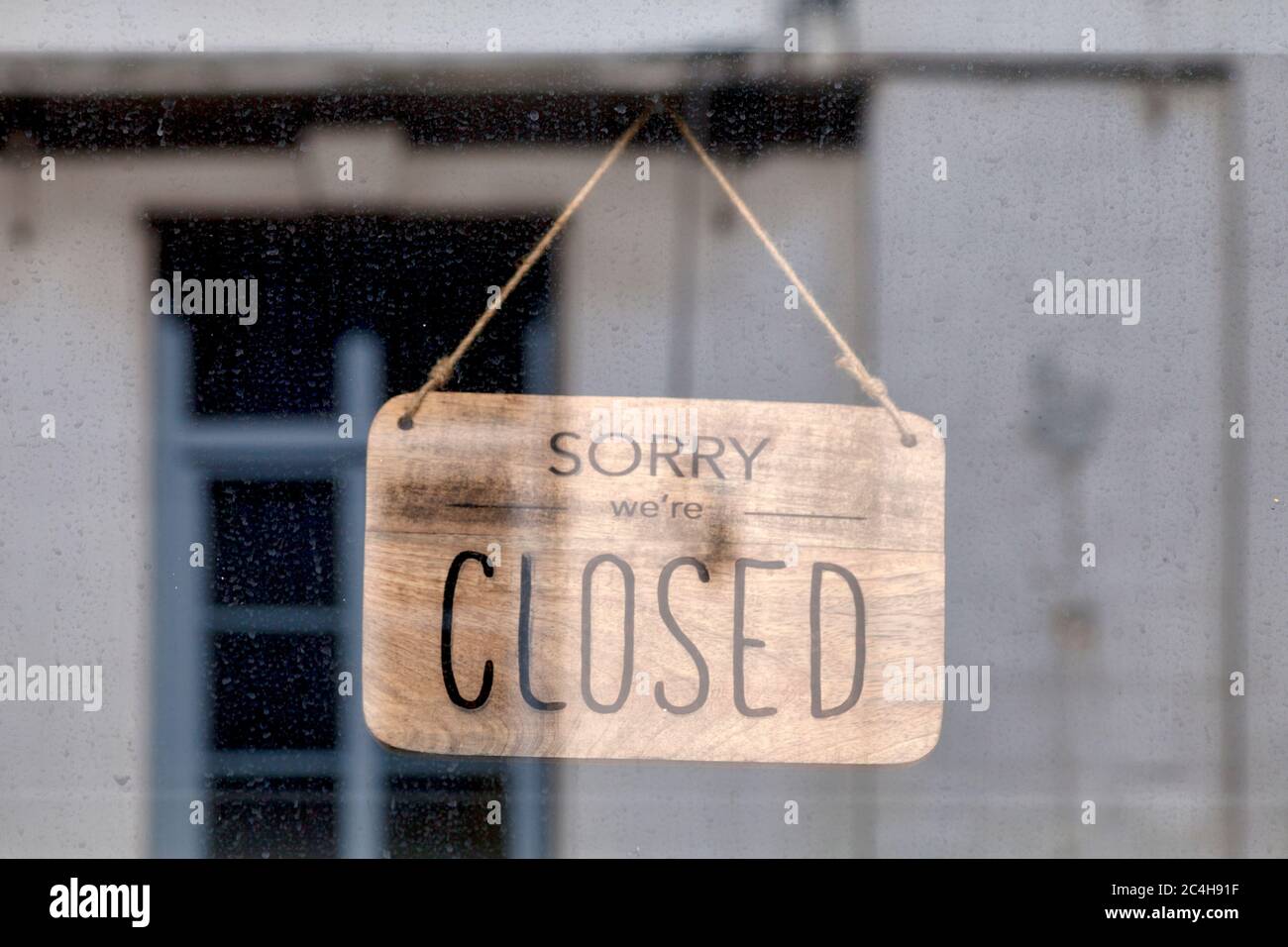 Wooden sign hanging at the glass door of a shop saying: Sorry, we're ...