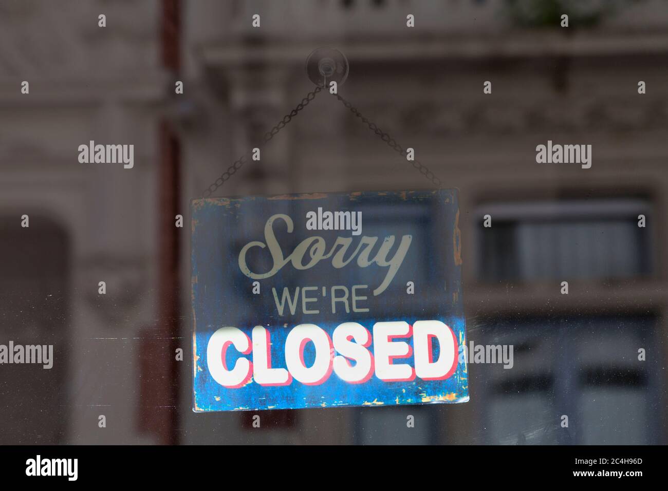 Black sign hanging at the glass door of a shop saying: Sorry, we're ...