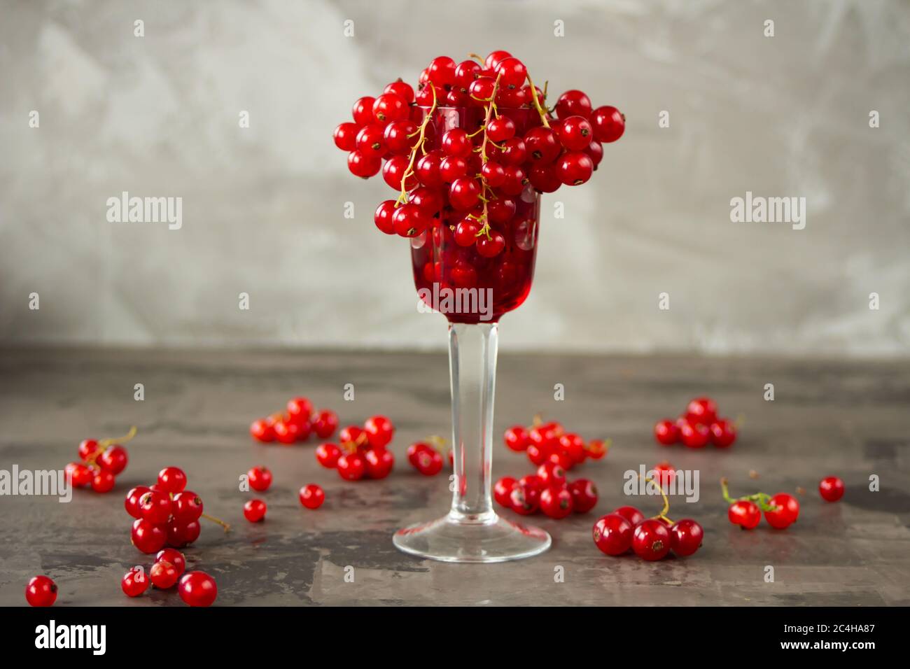 Red currant in a shot glass, the rest is scattered around it on a gray ...