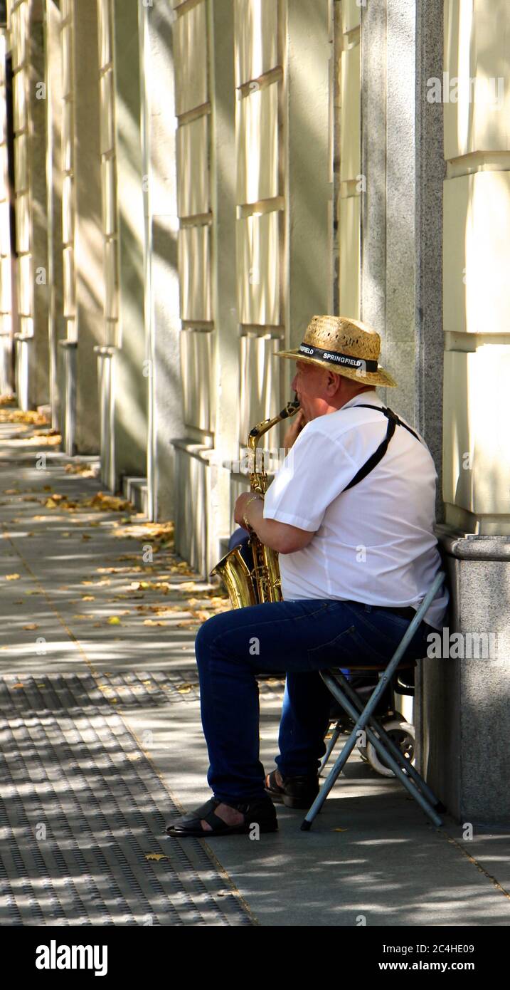 Saxophone playing busker sitting on a blue fold up chair on the Calle ...