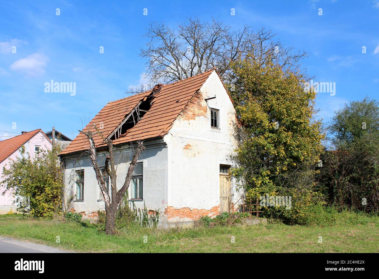 Abandoned small suburban family house ruins with destroyed roof and cracked facade surrounded ...