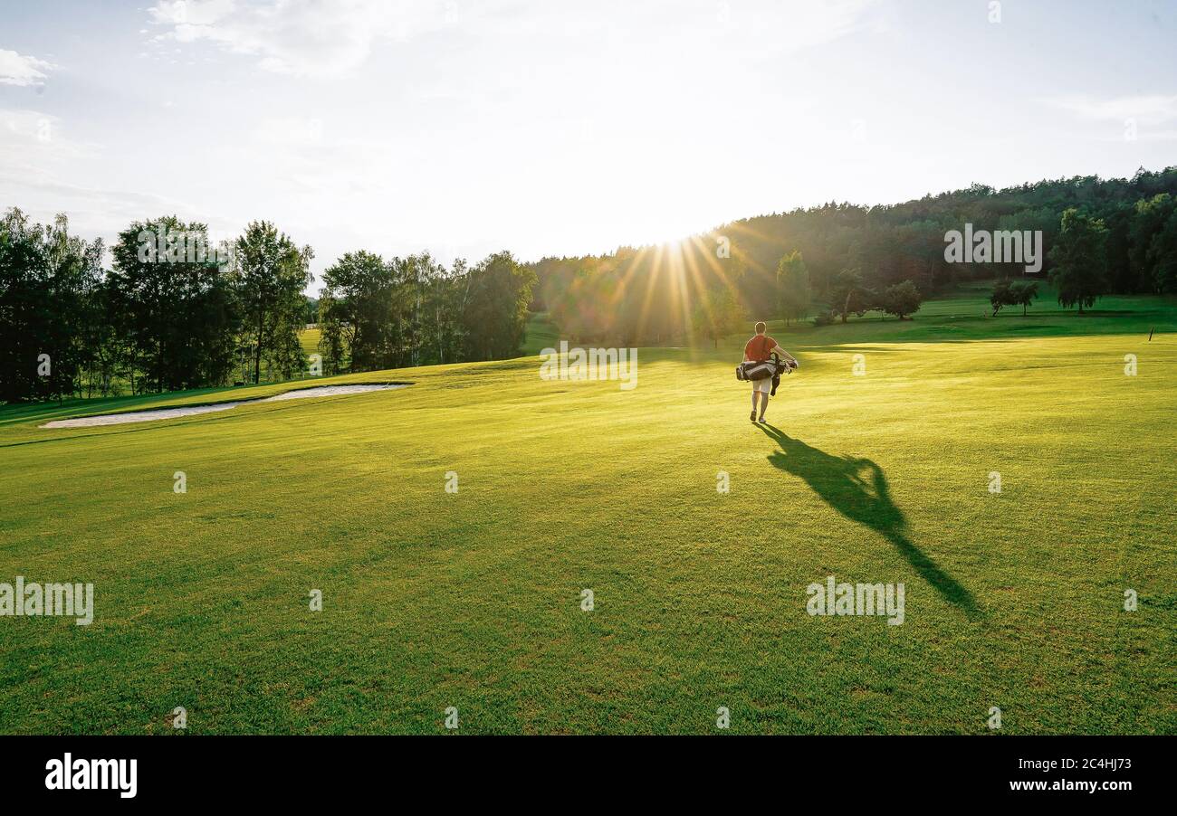 Handsome young golfer carrying a bag and walking to the next hole on a ...