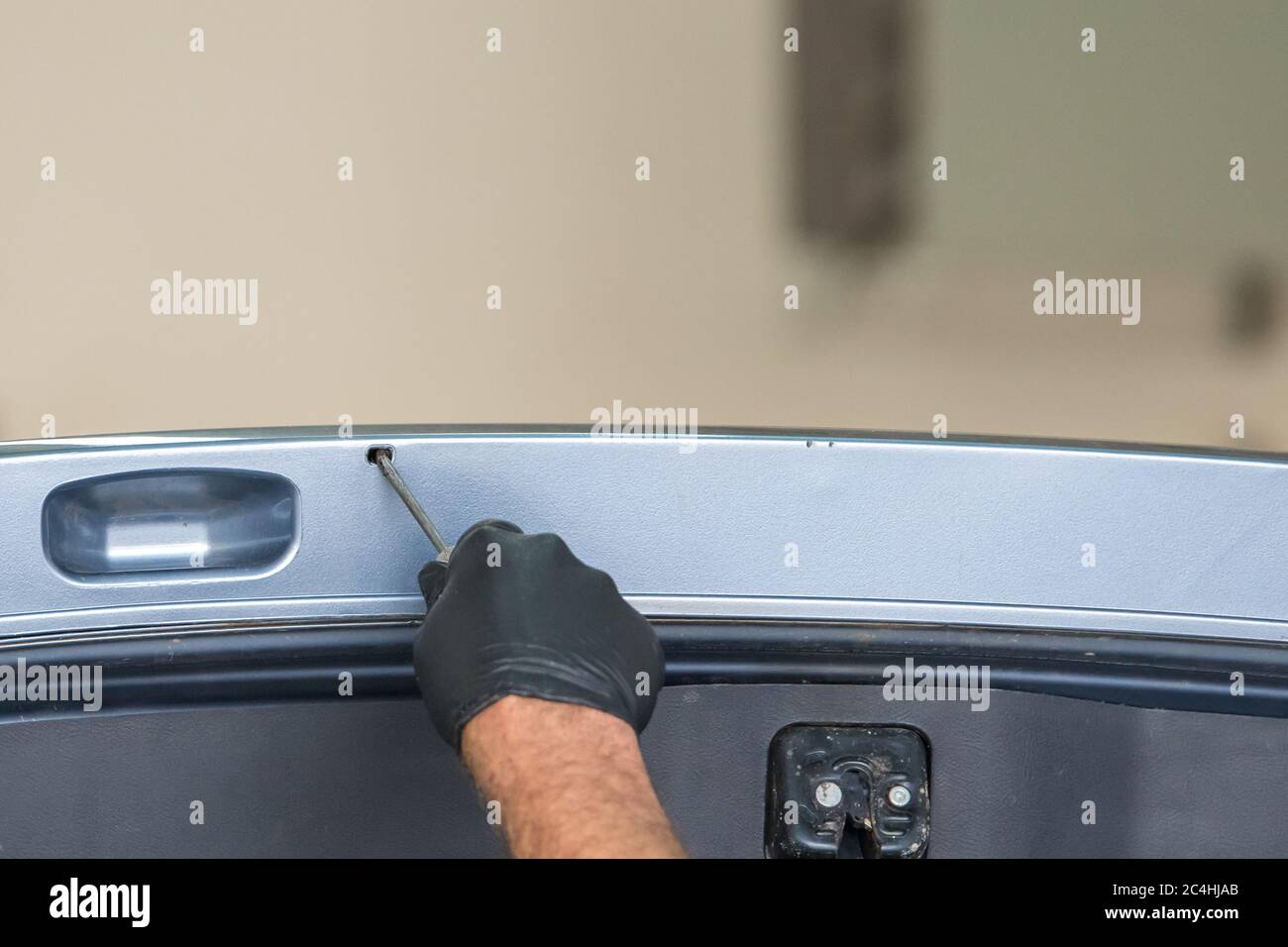 A gloved hand spraying rust proofing into a small hole in the hatch of ...