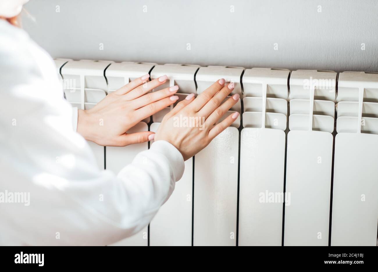 Woman warms up hands over heater Stock Photo - Alamy