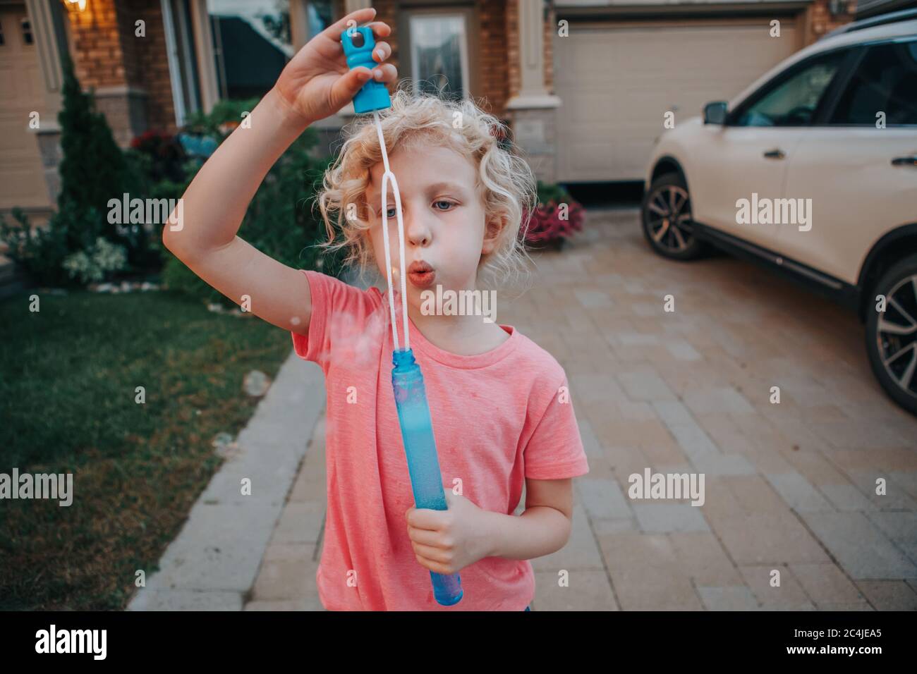 Young Caucasian girl blowing soap bubbles on home front yard. Child ...