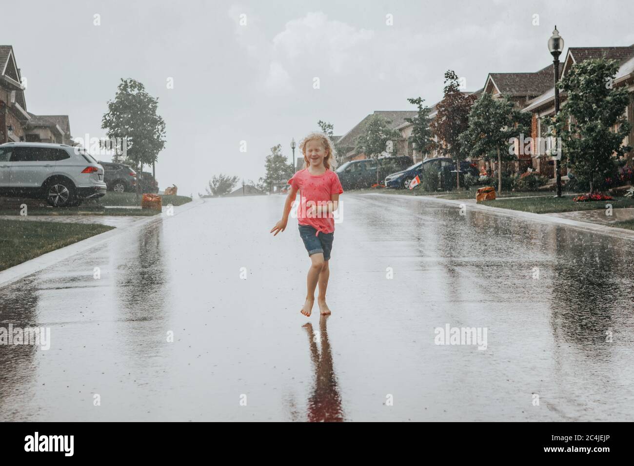 Cute adorable girl running splashing under rain on street road. Child ...
