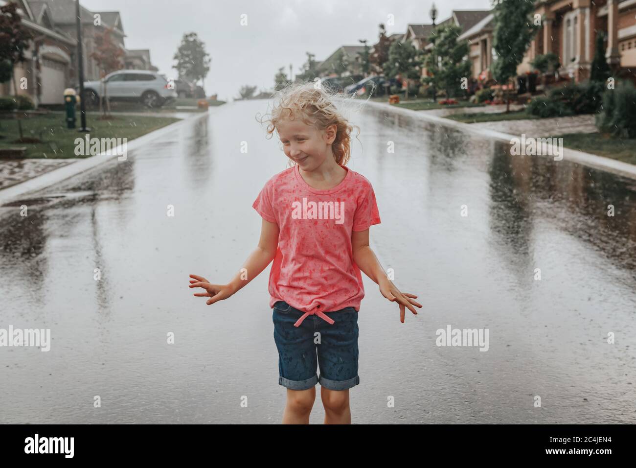 Cute adorable girl running splashing under rain on street road. Child ...