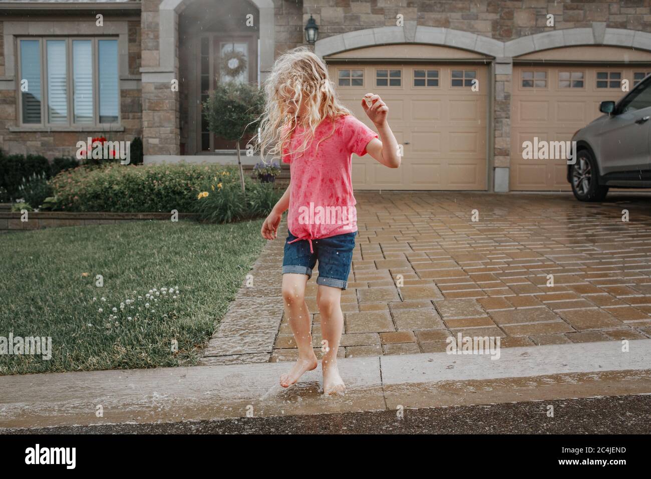 Cute adorable girl running splashing under rain on street road. Child ...