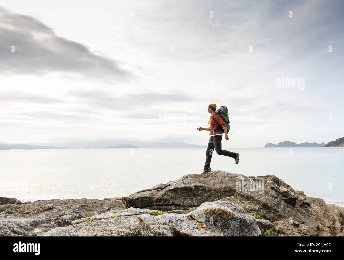 Man with backpack running over the rocks Stock Photo - Alamy