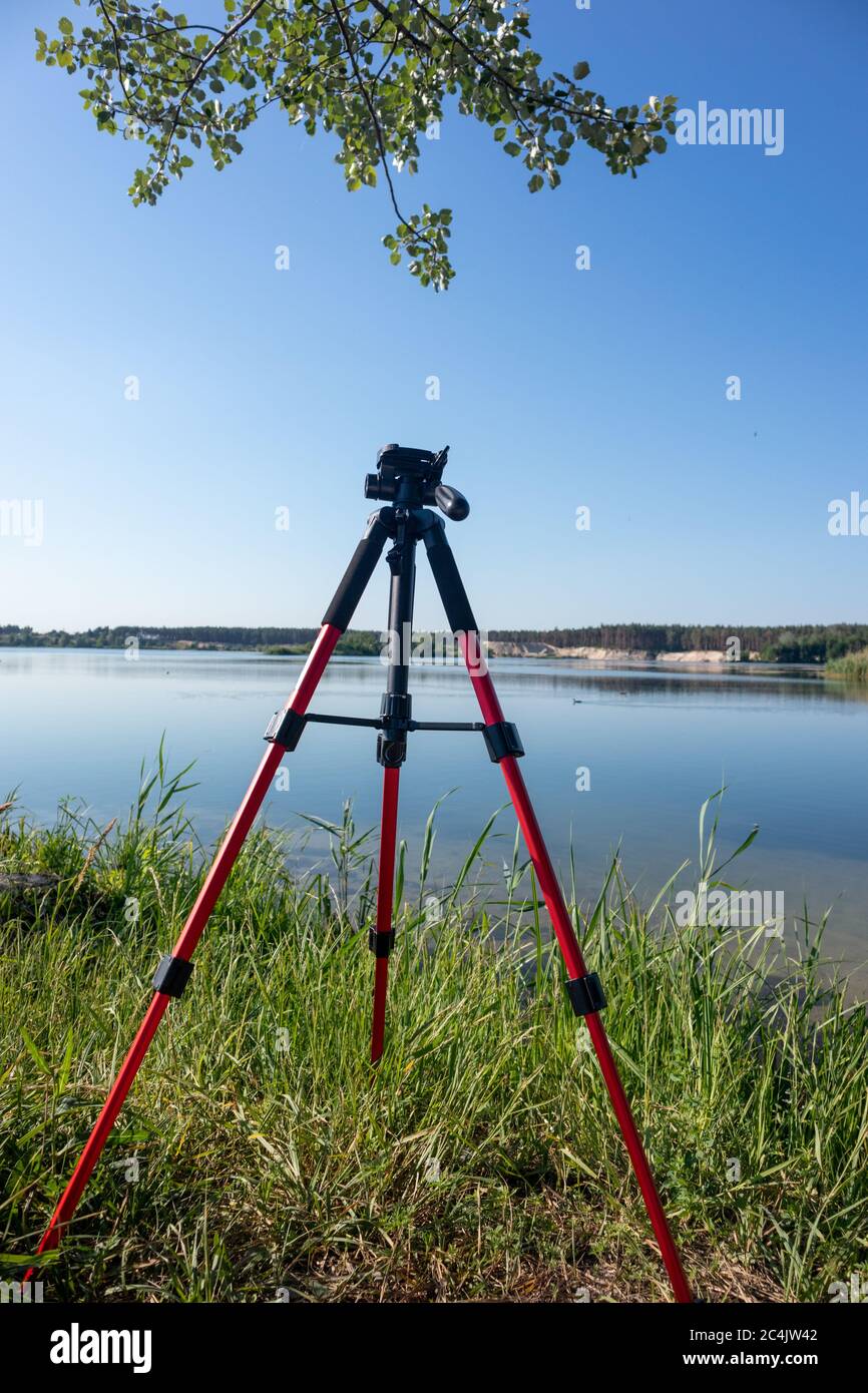 Camera red tripod standing in green grass near lake water natural ...