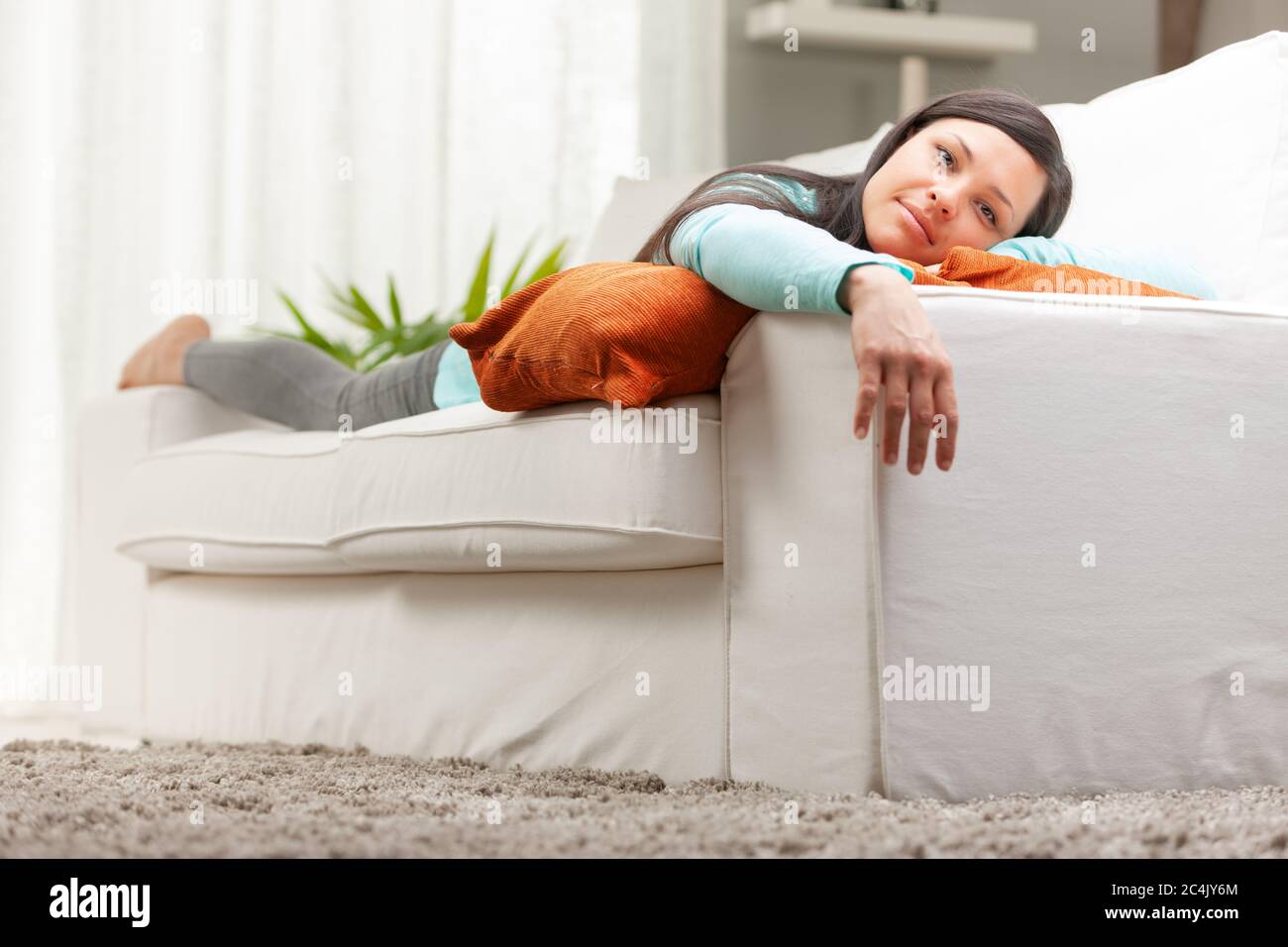 woman easing down on her couch in a white living room Stock Photo - Alamy