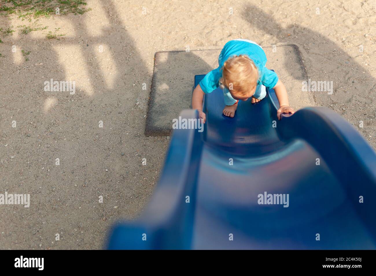Child playing and climbing a blue slide at a playground Stock Photo - Alamy