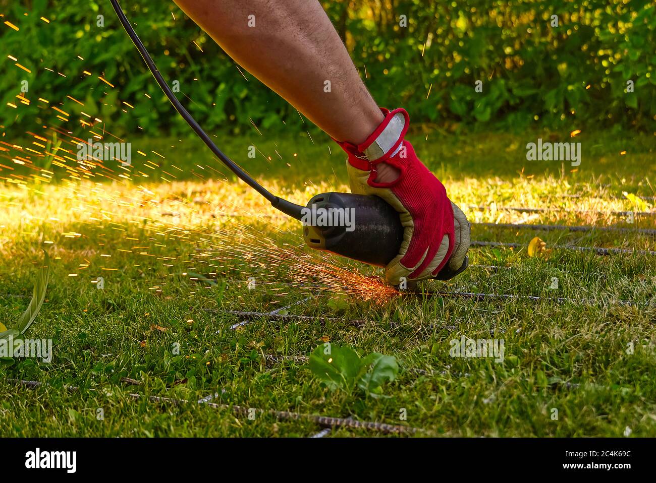 Cutting metal net with grinder on green grass. Sparks from contact ...