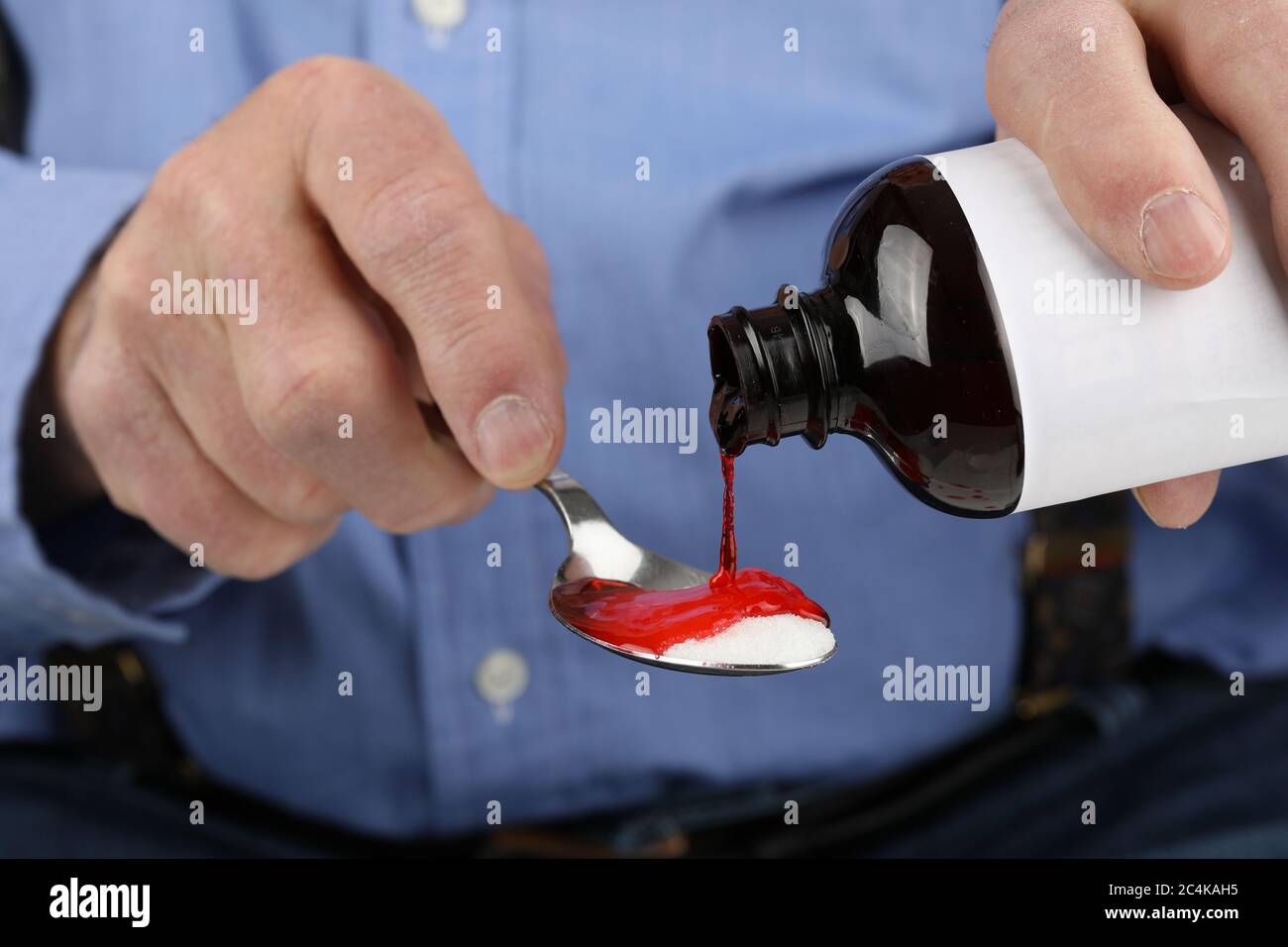 an elderly man pouring red medicine onto a spoon full of sugar to hide ...