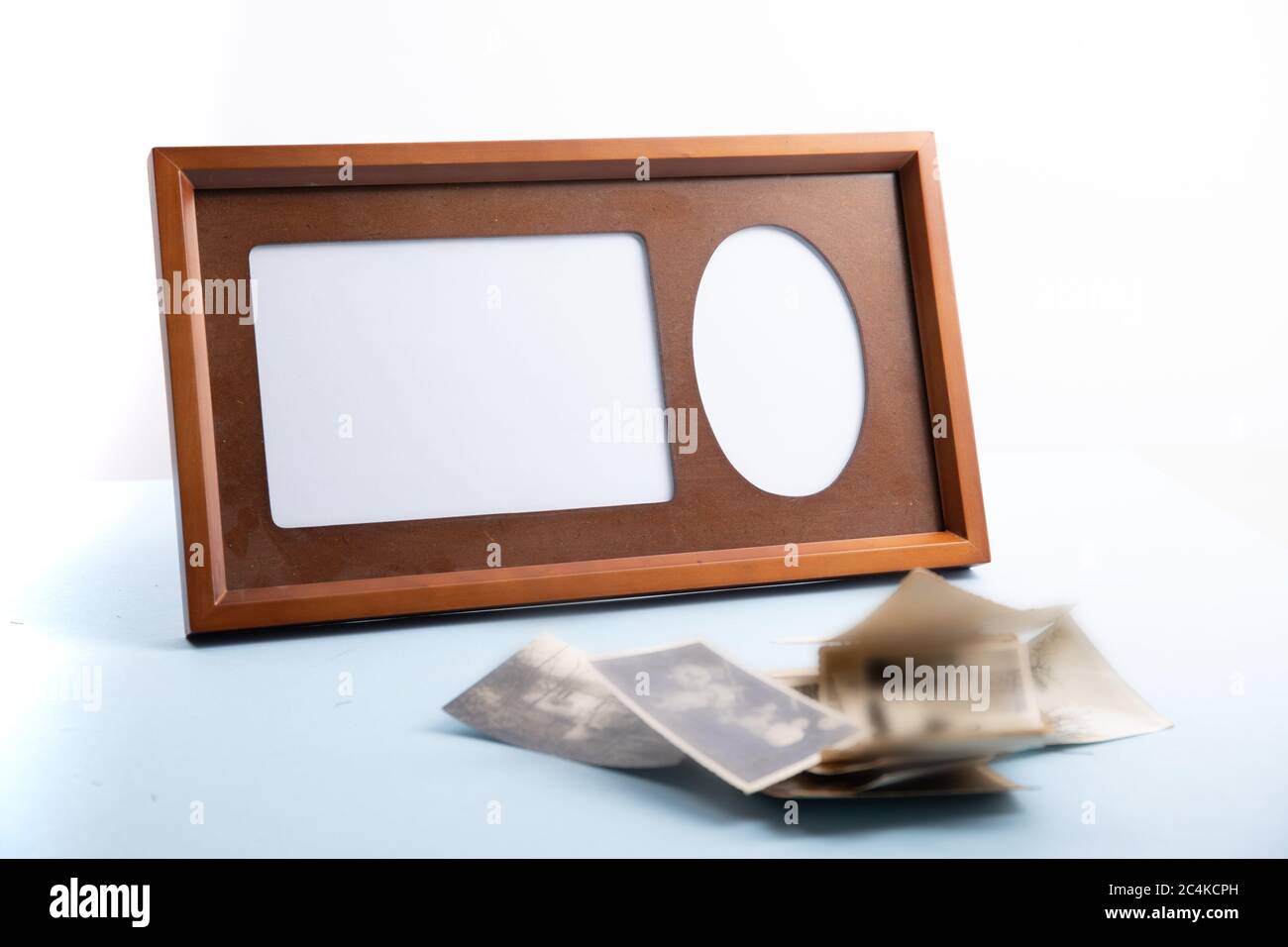 an empty wooden photo frame and mat with a pile of old photos on a blue ...
