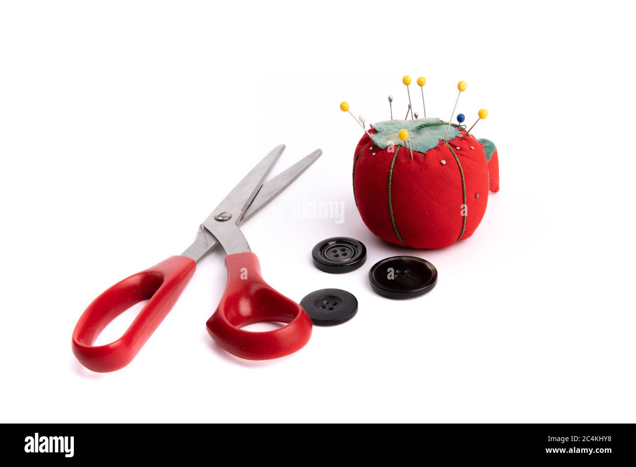 a red pin cushion with black buttons and tailoring scissors isolated on ...