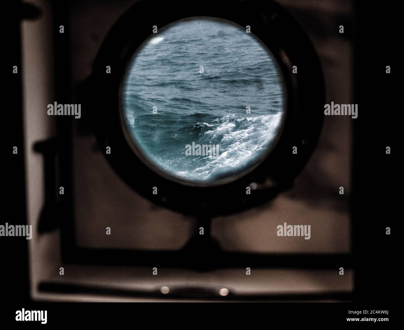 Round ship window with brown edges and the wavy sea seen through it ...