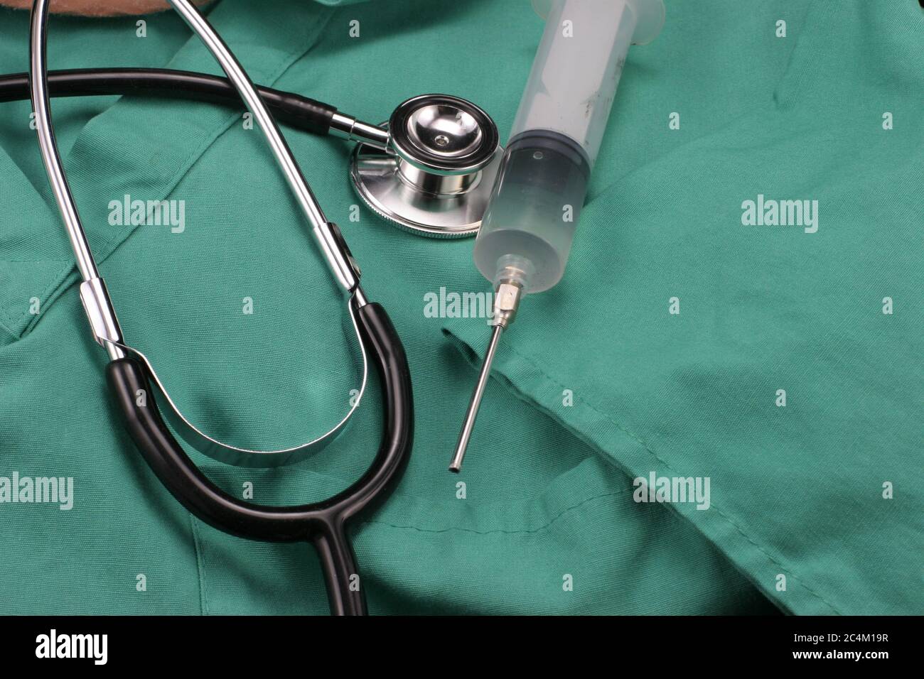 Medical stethoscope.with large injection needle on top of green scrubs ...