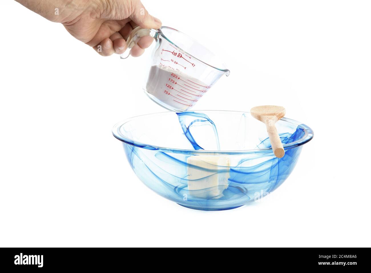 a baker's hand pouring flour into a blue glass mixing bowl with butter ...