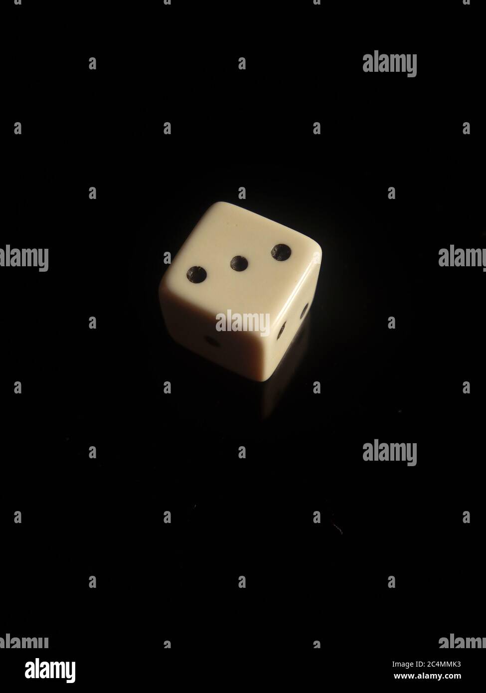 Vertical shot of white dice showing three pips isolated on a black ...