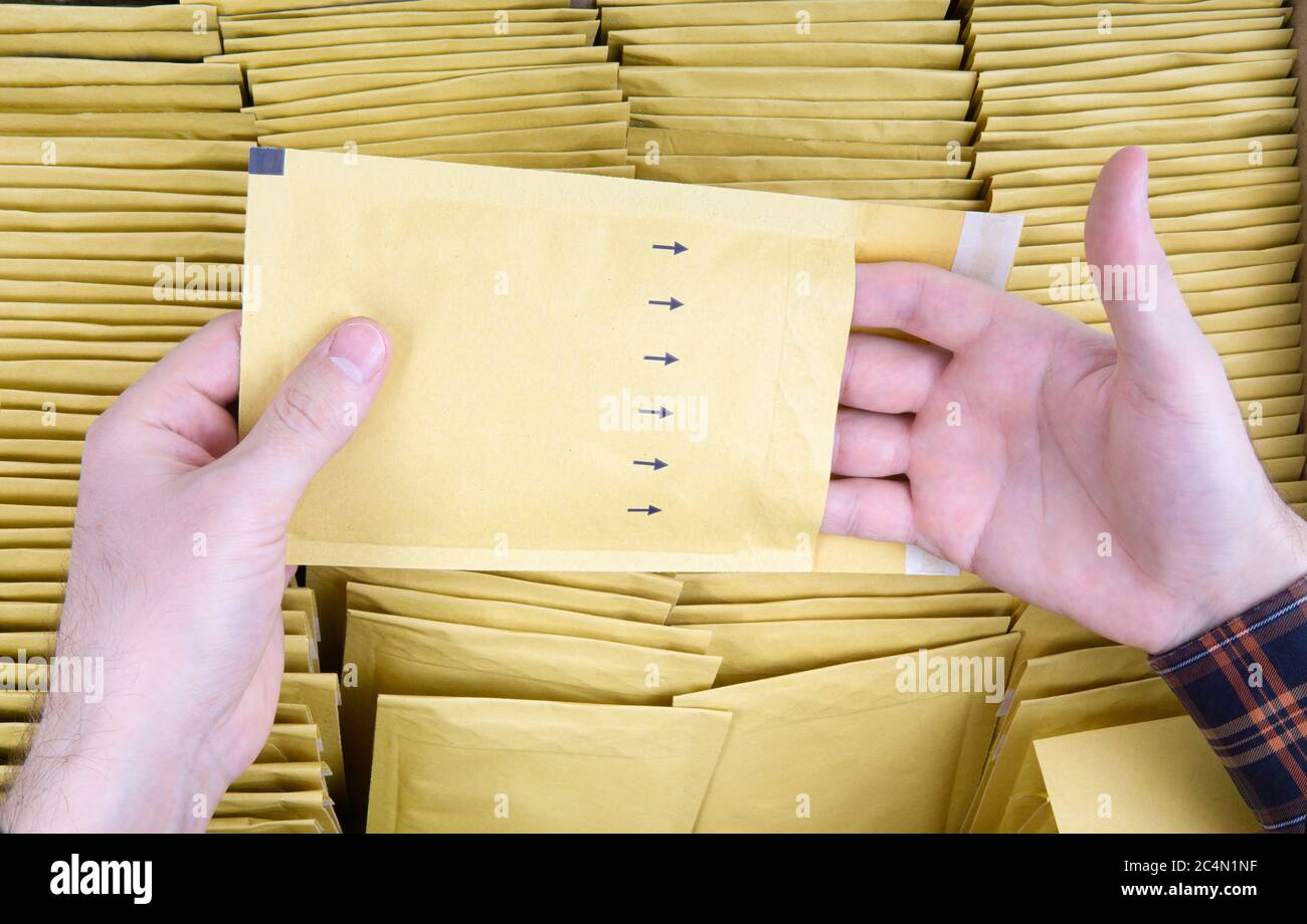 Male hands open a yellow bubble envelope against the open shipping box ...
