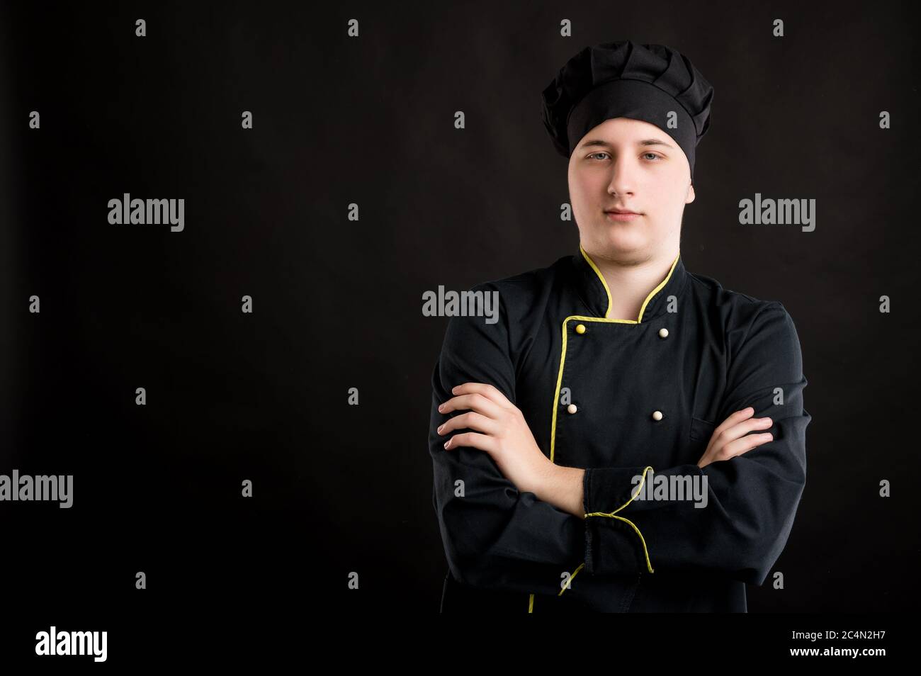 Portrait of young male dressed in a black chef suit looking confident ...