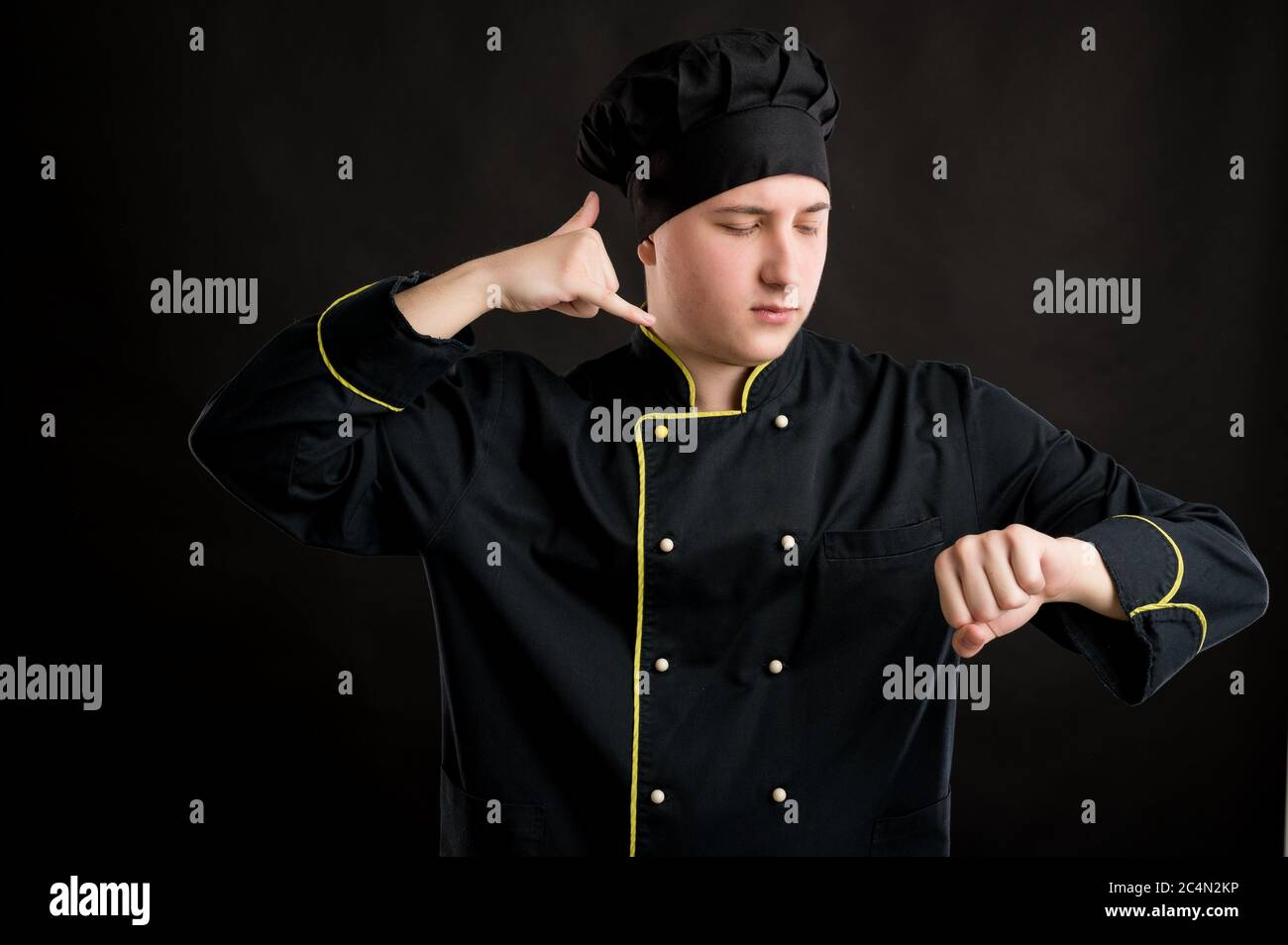 Portrait of young male dressed in a black chef suit showing it's time ...