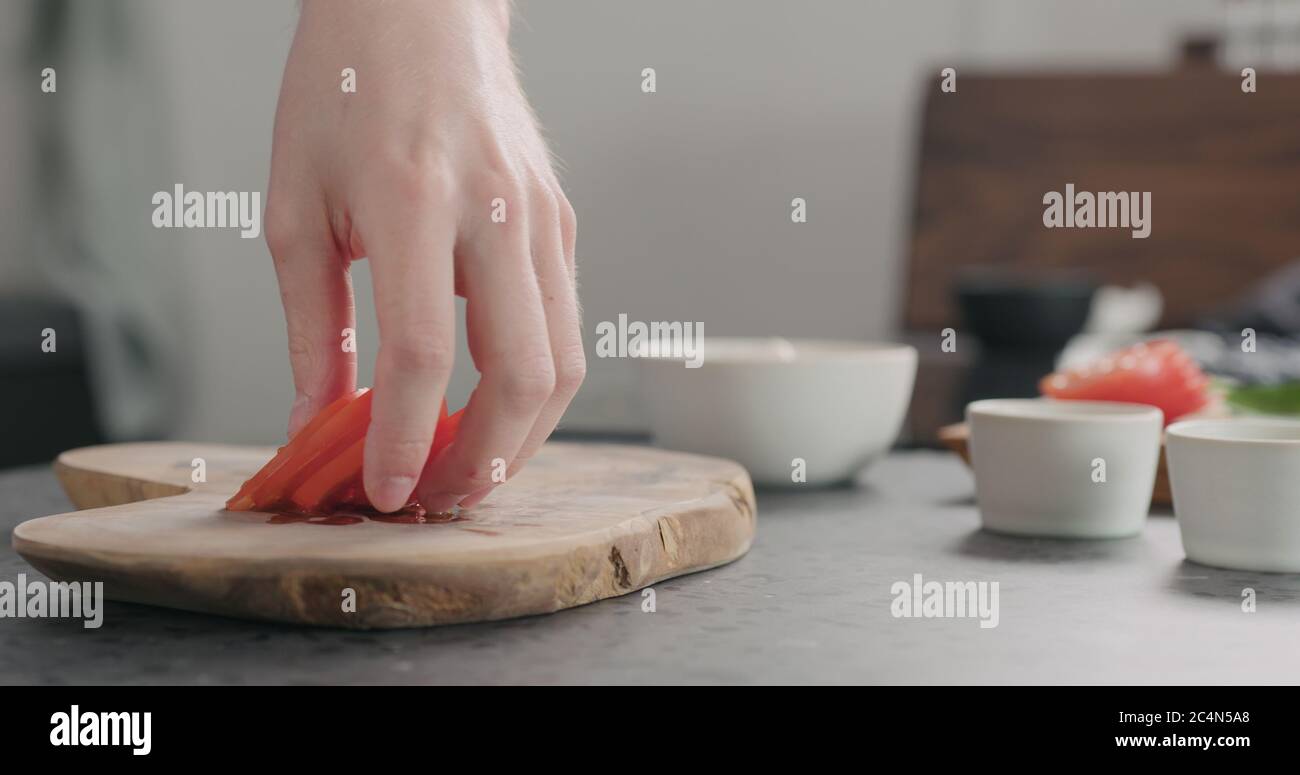 man take sliced tomato from olive wood board Stock Photo - Alamy
