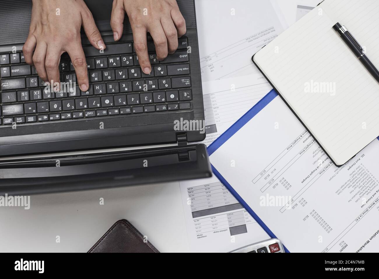Overhead shot of a person typing on the laptop next to other documents ...