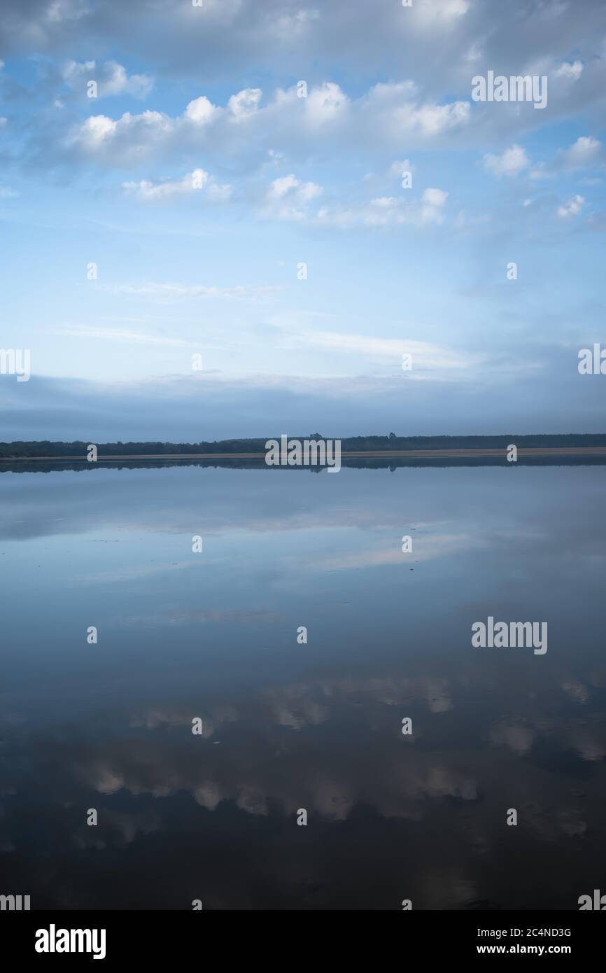 Vertical shot of a reflective lake surface on a cloudy sky background ...