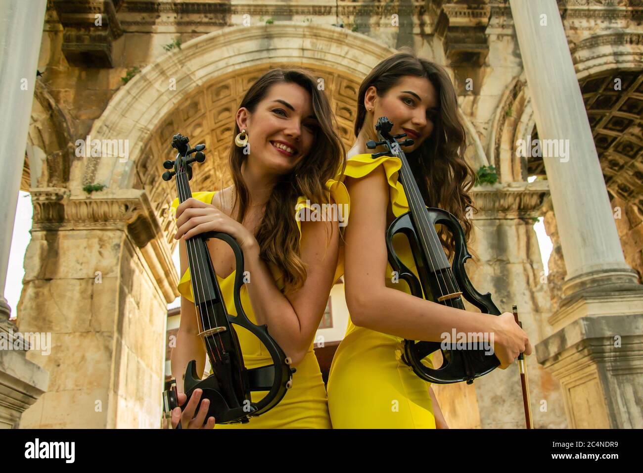 Two beautiful twin sisters violinists in yellow concert dresses are ...