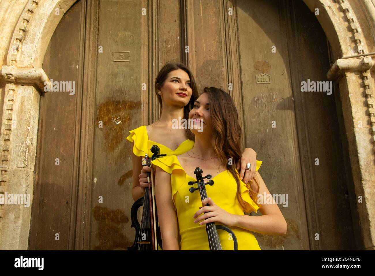 Two beautiful twin sisters violinists in yellow concert dresses are ...