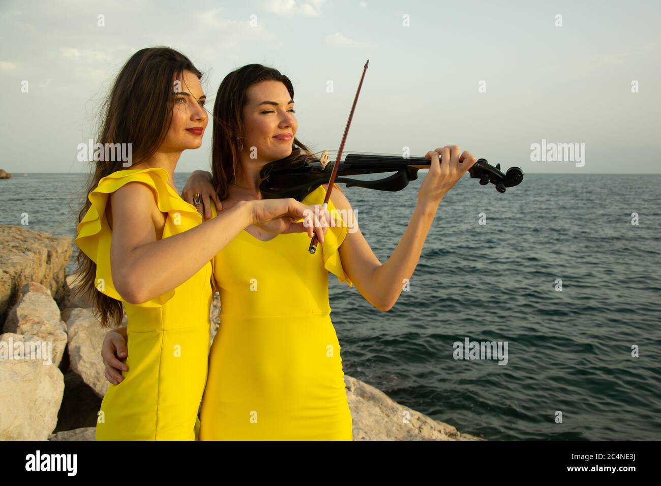 Two beautiful girls violinists in yellow concert dresses are playing ...