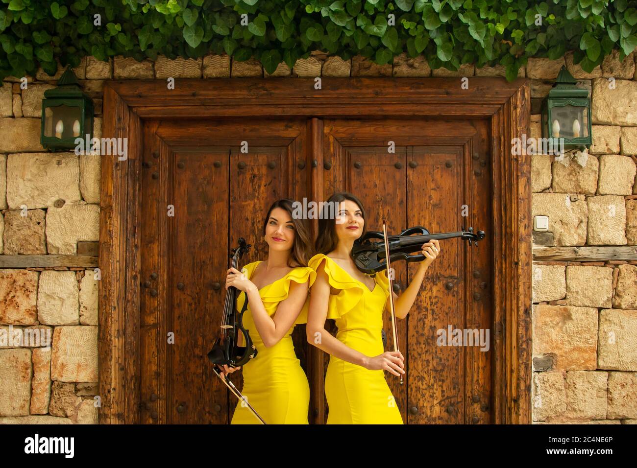 Two beautiful twin sisters violinists in yellow concert dresses are ...
