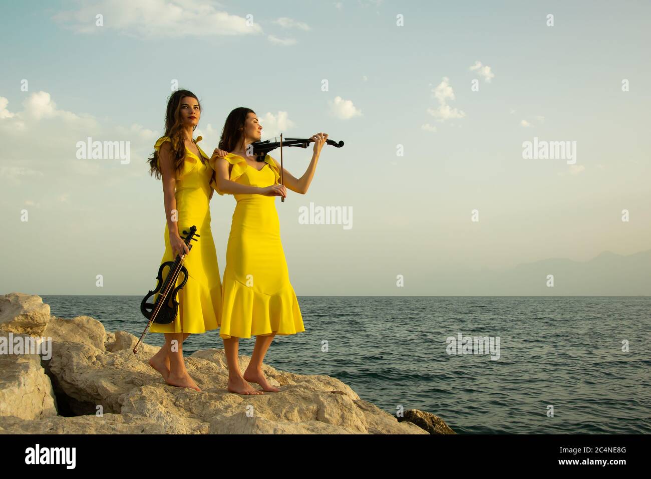 Two beautiful twin sisters violinists in yellow concert dresses are ...