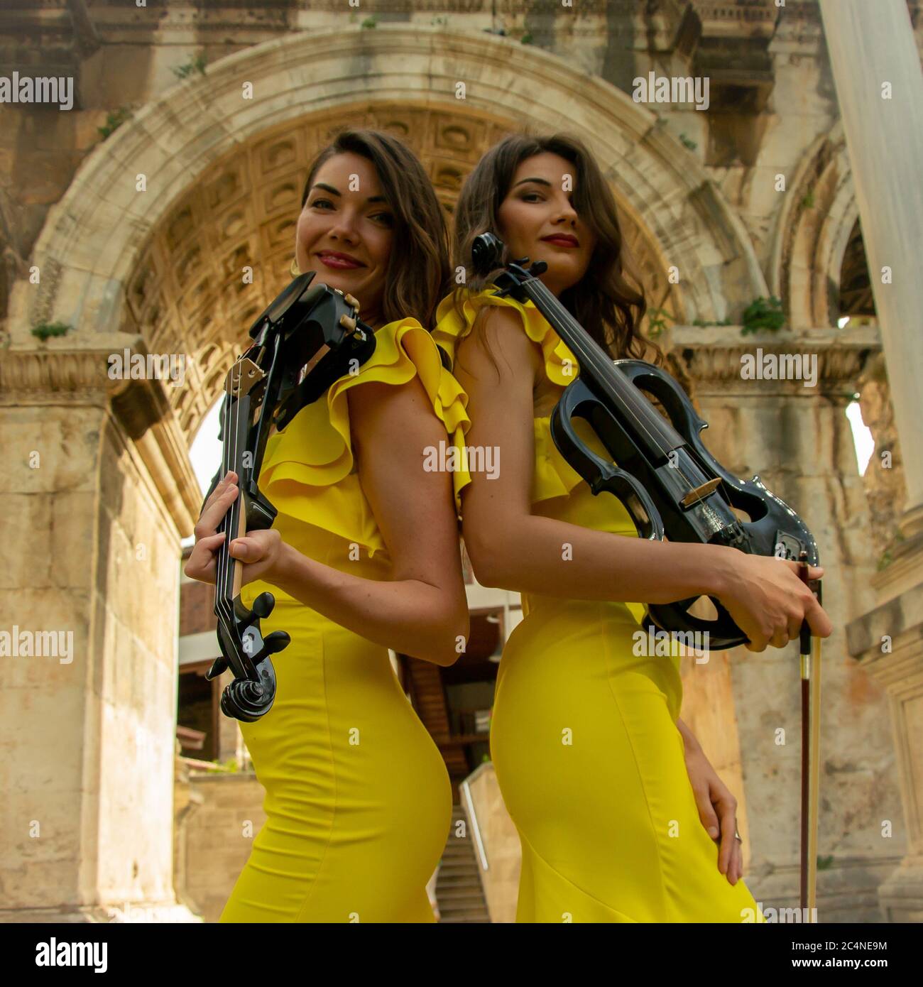 Two beautiful twin sisters violinists in yellow concert dresses are ...