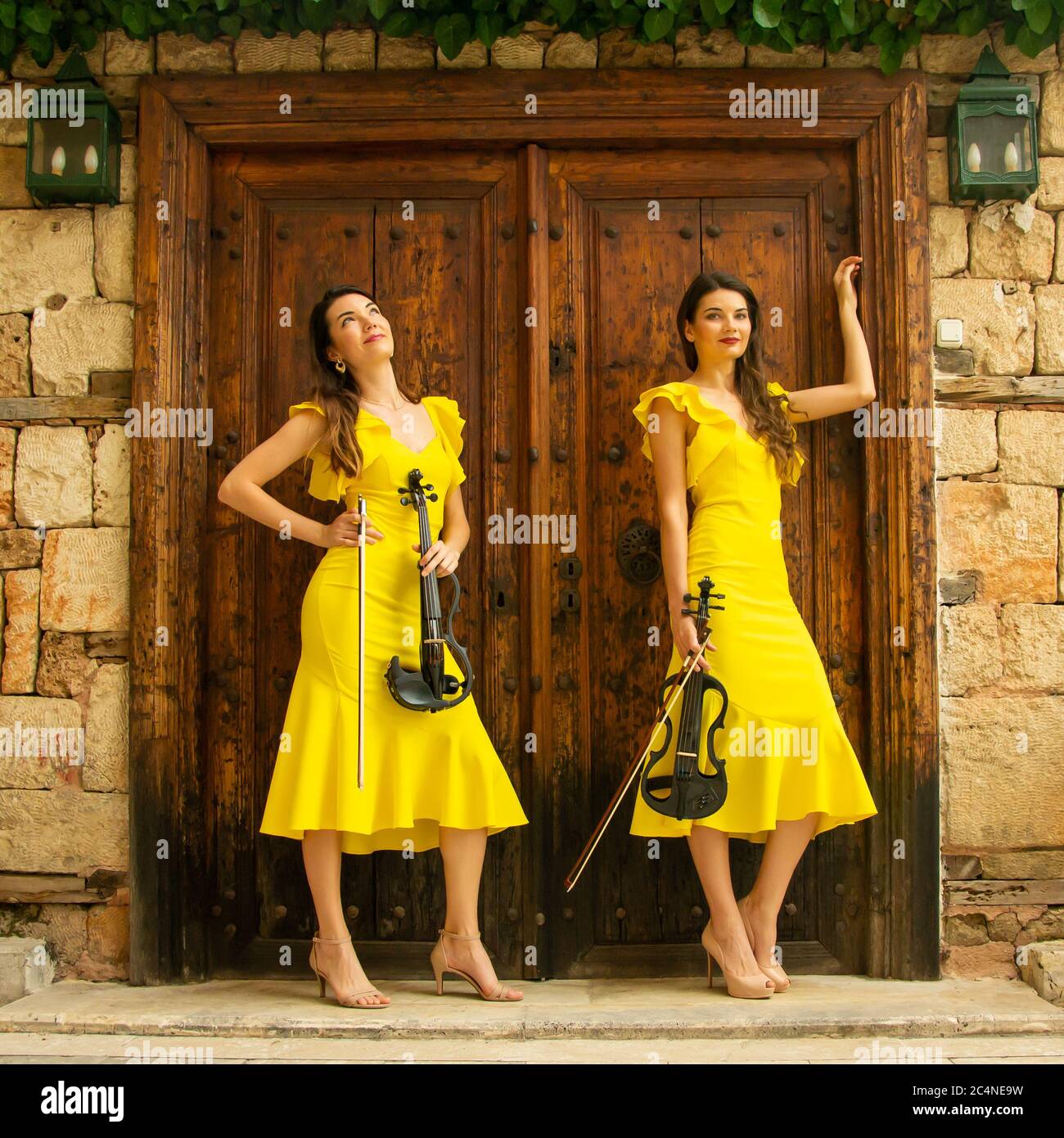 Two beautiful twin sisters violinists in yellow concert dresses are ...