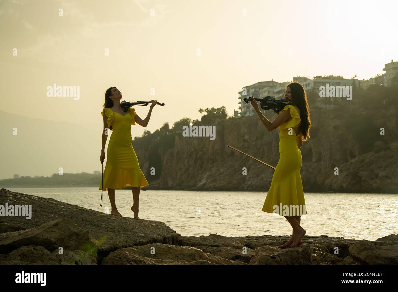 Two beautiful twin sisters violinists in yellow concert dresses are ...