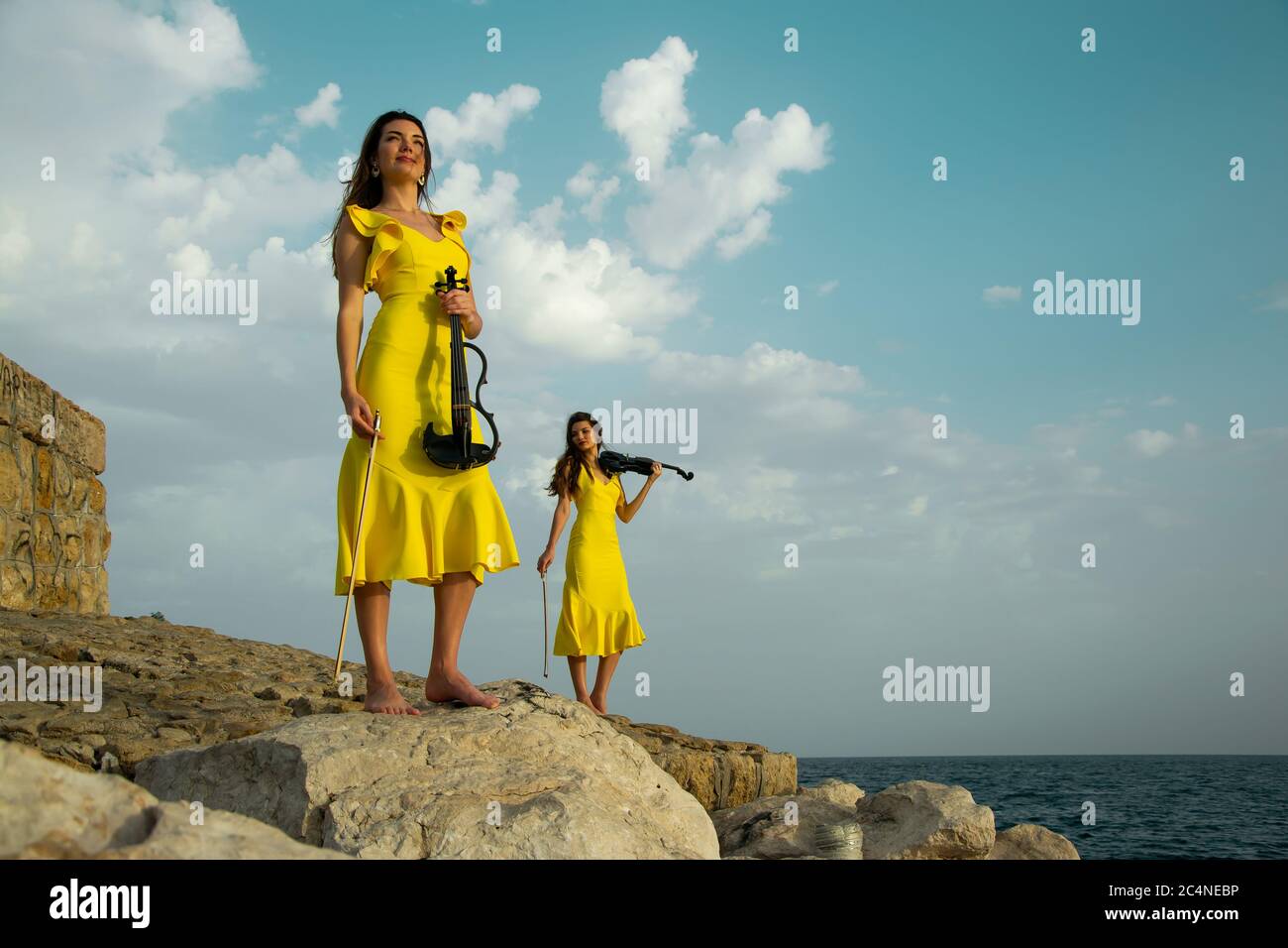 Two beautiful twin sisters violinists in yellow concert dresses are ...