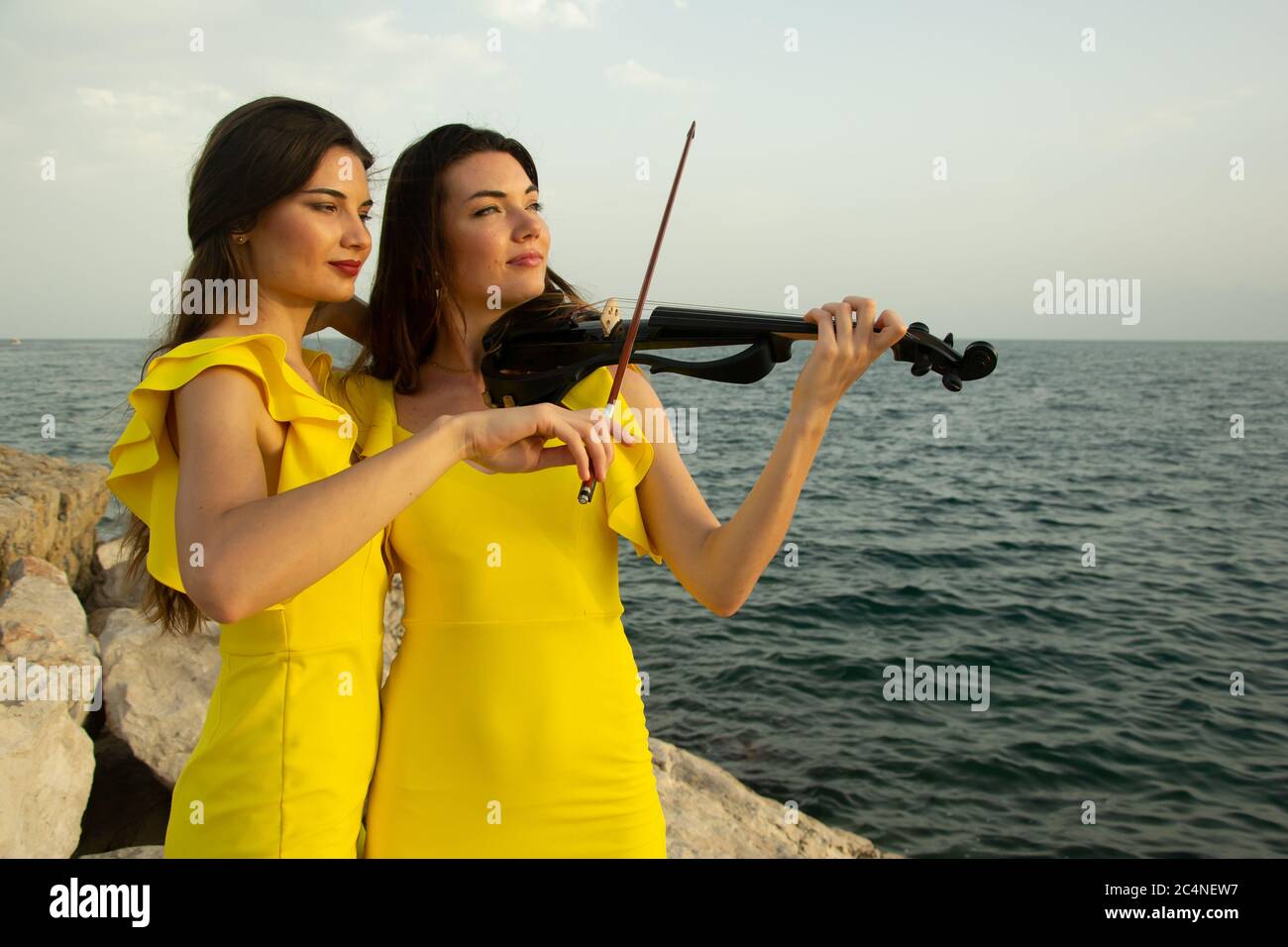 Two beautiful girls violinists in yellow concert dresses are playing ...