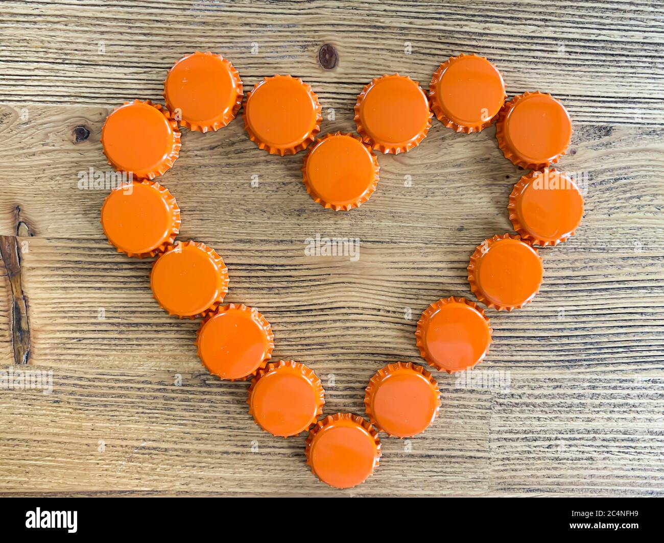 An orange love heart made from beer bottle tops lids on a rustic wooden ...