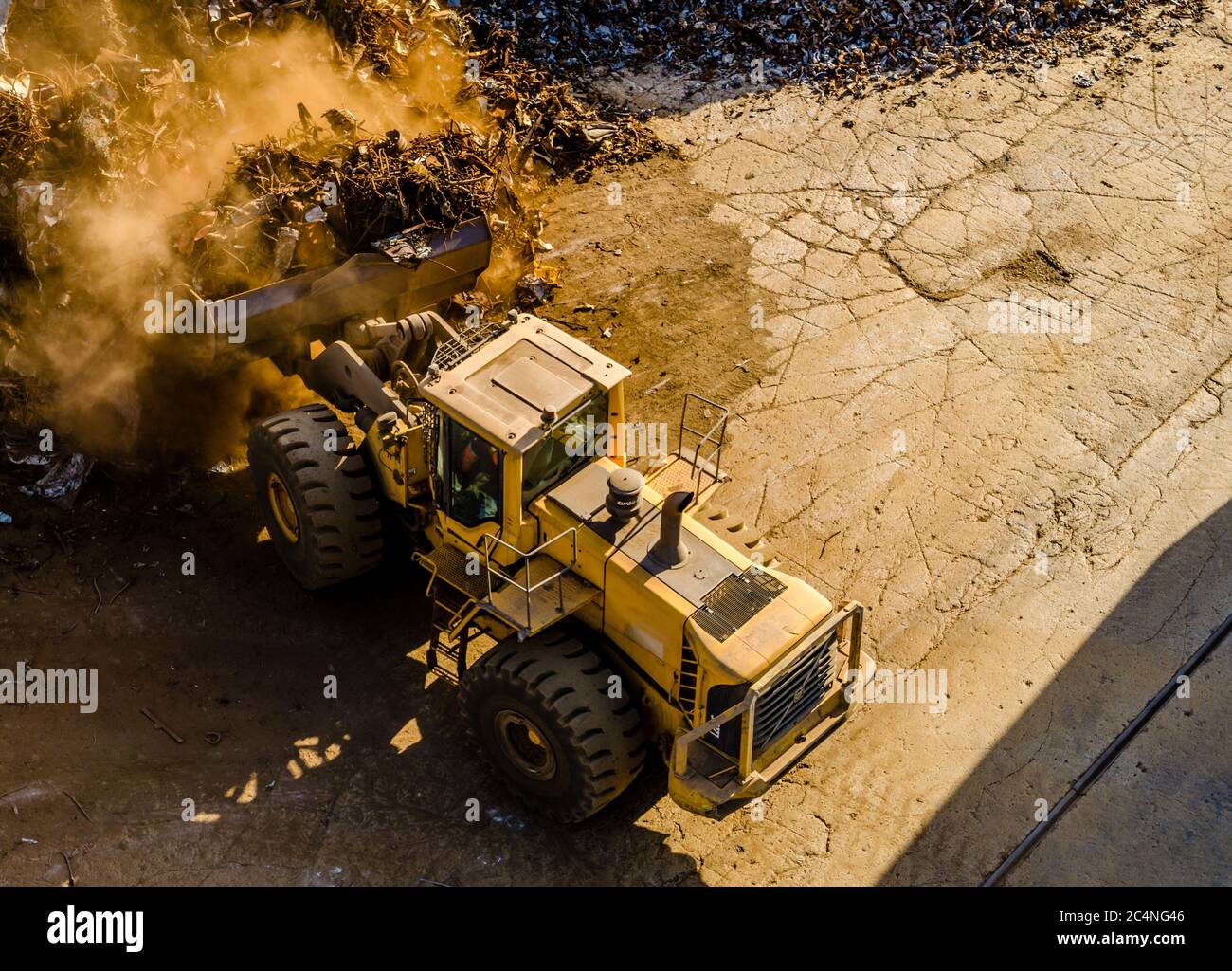 Horizontal shot of a yellow front loader tractor carrying dusty waste ...