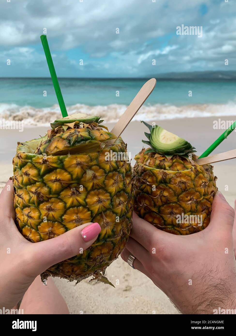 Two caucasian hands holding a pina colada cocktail in pineapple with ...