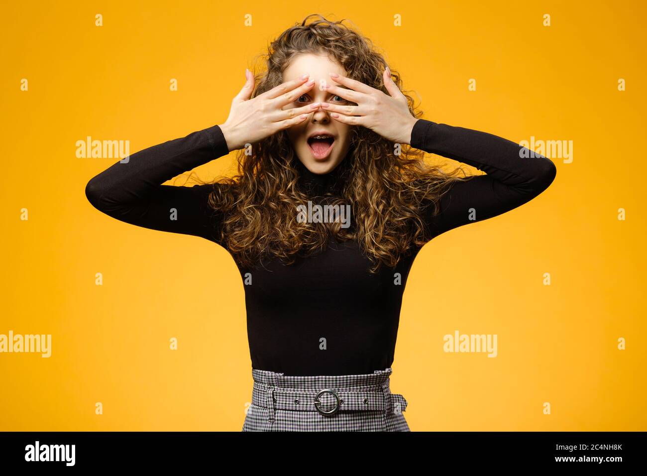Pretty girl hide her face with hands isolated on yellow background ...