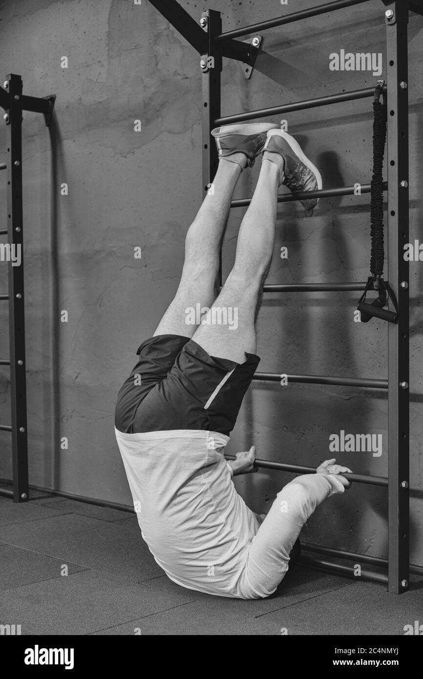 Athletic young man doing exercise for abdomen on vertical bar in gym or ...