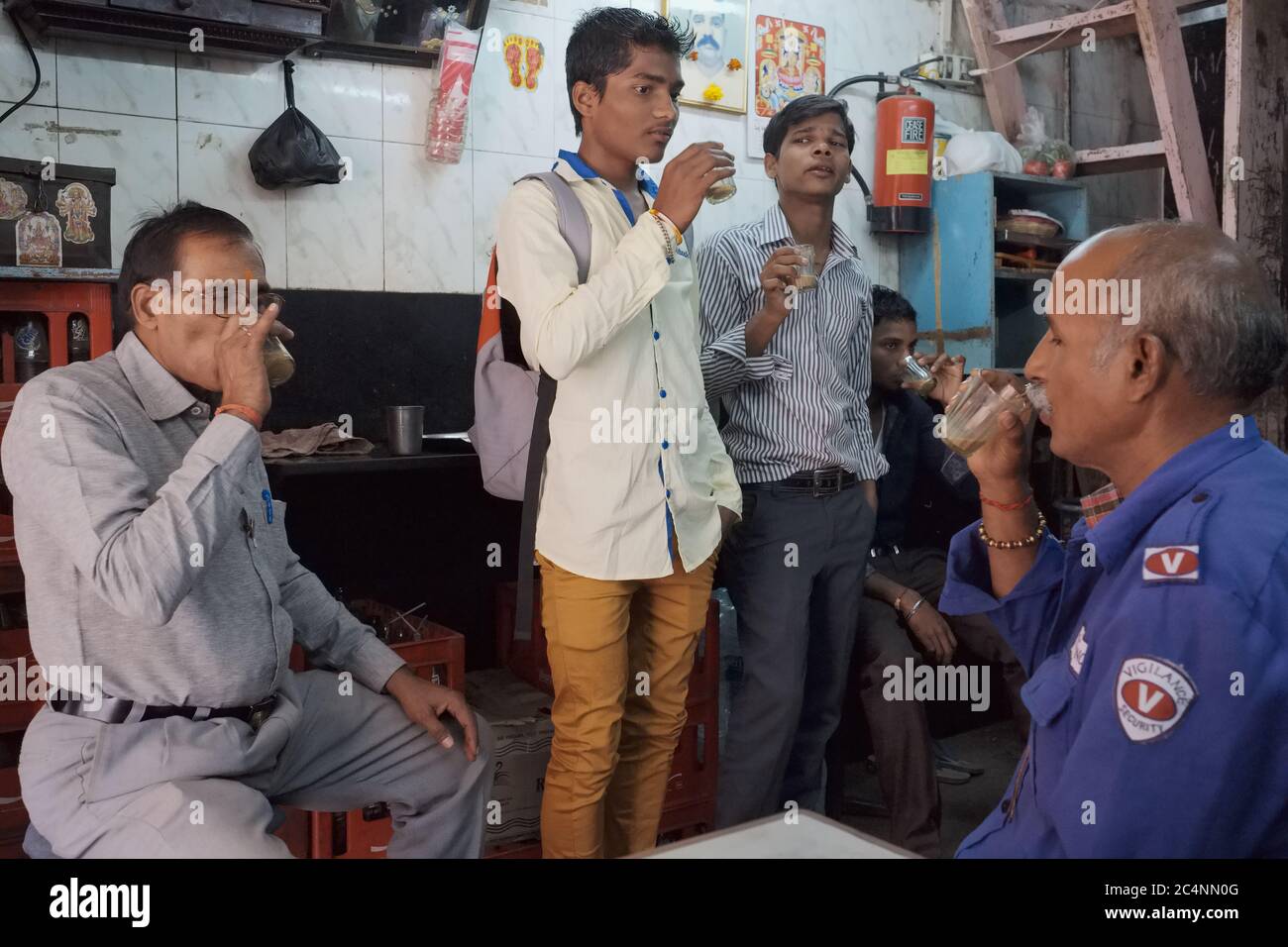 Customers in a small tea shop in Mumbai, India, drinking their glasses ...