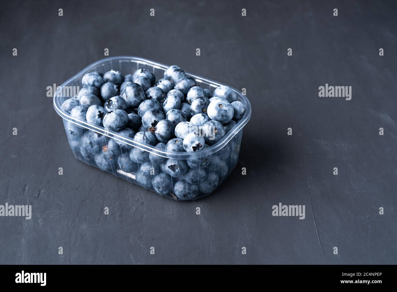 Tasty juicy raw blueberries in a plastic container on a black dark ...